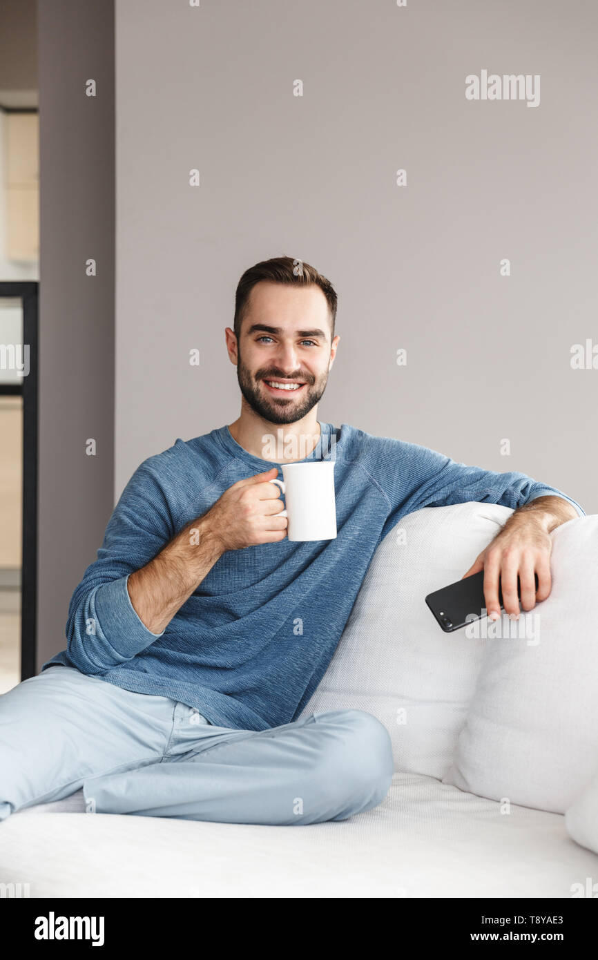 Attractive young man relaxing on a couch at home, using mobile phone ...
