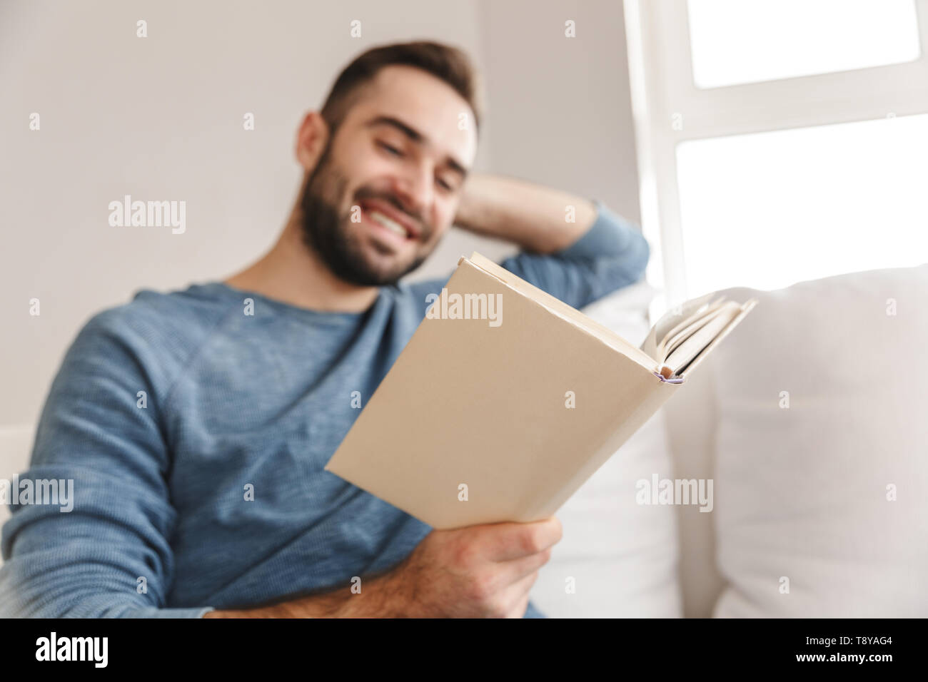 Attractive young man relaxing on a couch at home, reading a book Stock ...