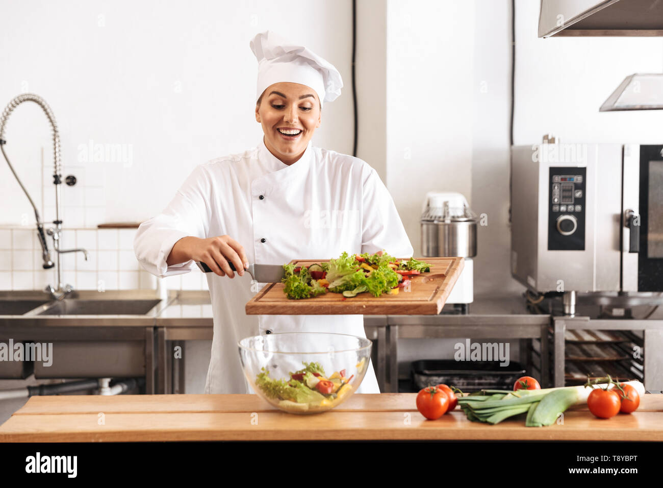 Photo of lovely woman chief wearing white uniform making salad with ...