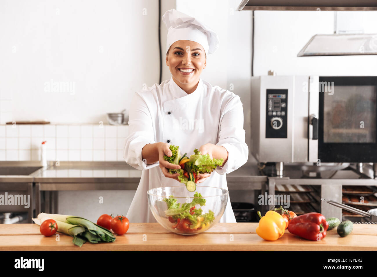 Photo of adult woman chief wearing white uniform making salad with ...