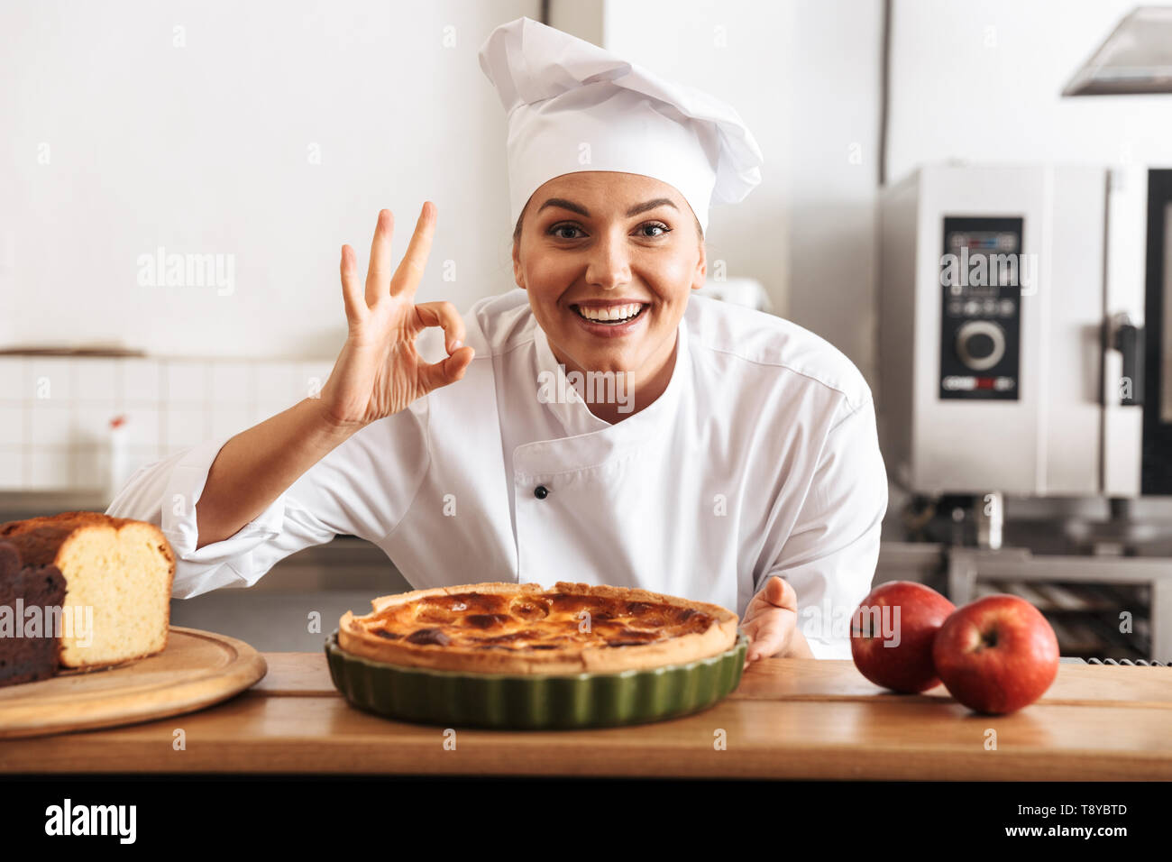 Image of smiling woman chef wearing white uniform posing in kitchen at ...