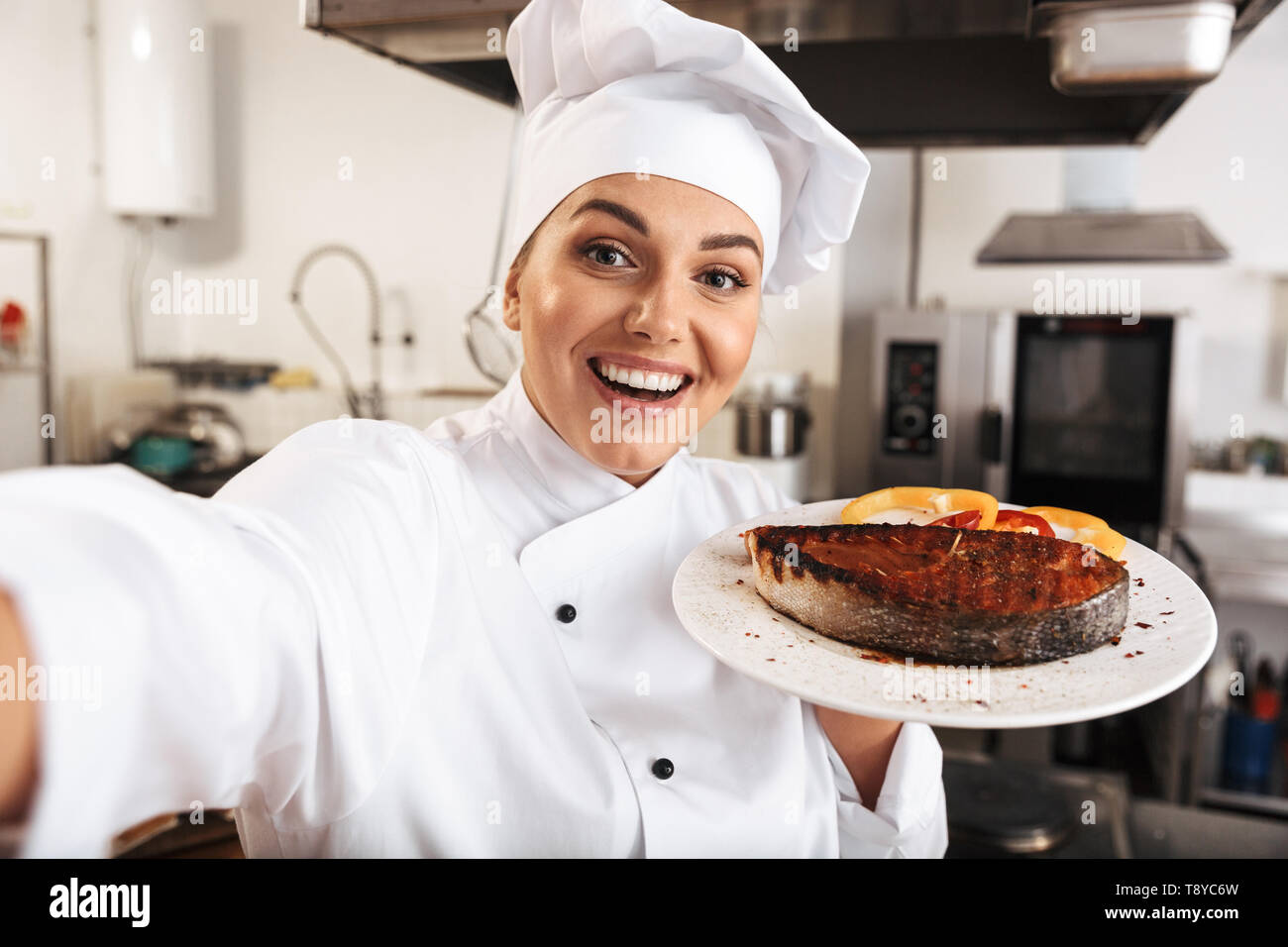 Portrait of smiling woman chef wearing white uniform taking selfie ...
