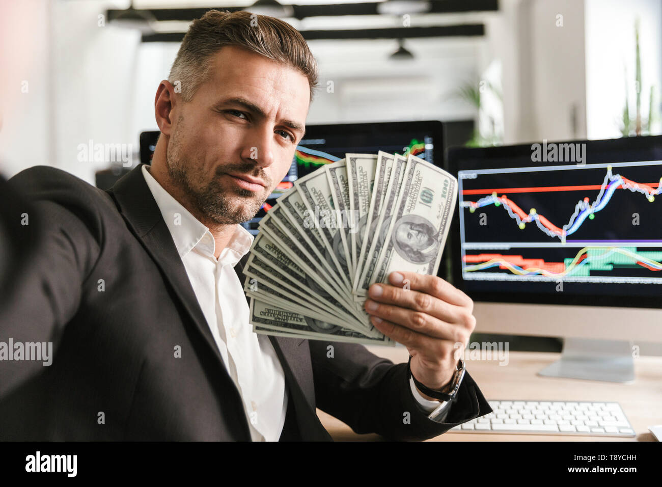 Image of rich businessman 30s wearing suit holding money fan while ...