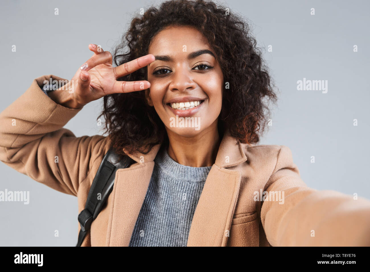Cheerful young african woman wearing coat walking outdoors, taking a selfie Stock Photo - Alamy