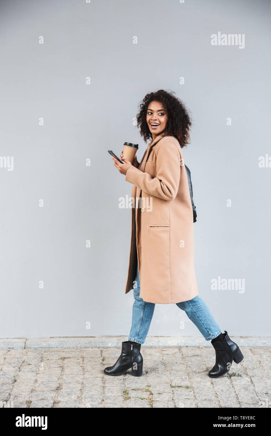 Full Length Of A Cheerful Young African Woman Wearing Coat Walking