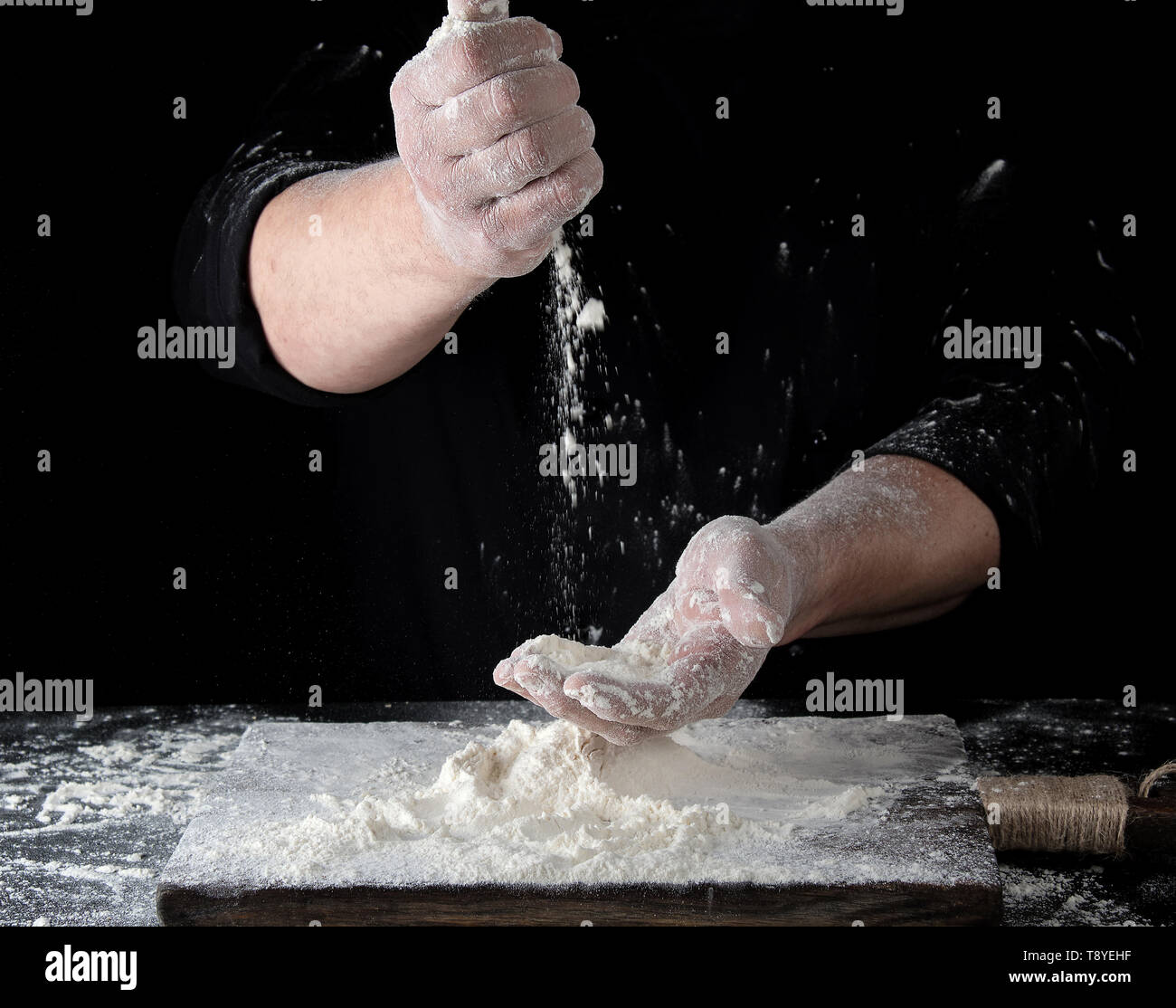 chef in black uniform sifts through his fingers white wheat flour over ...