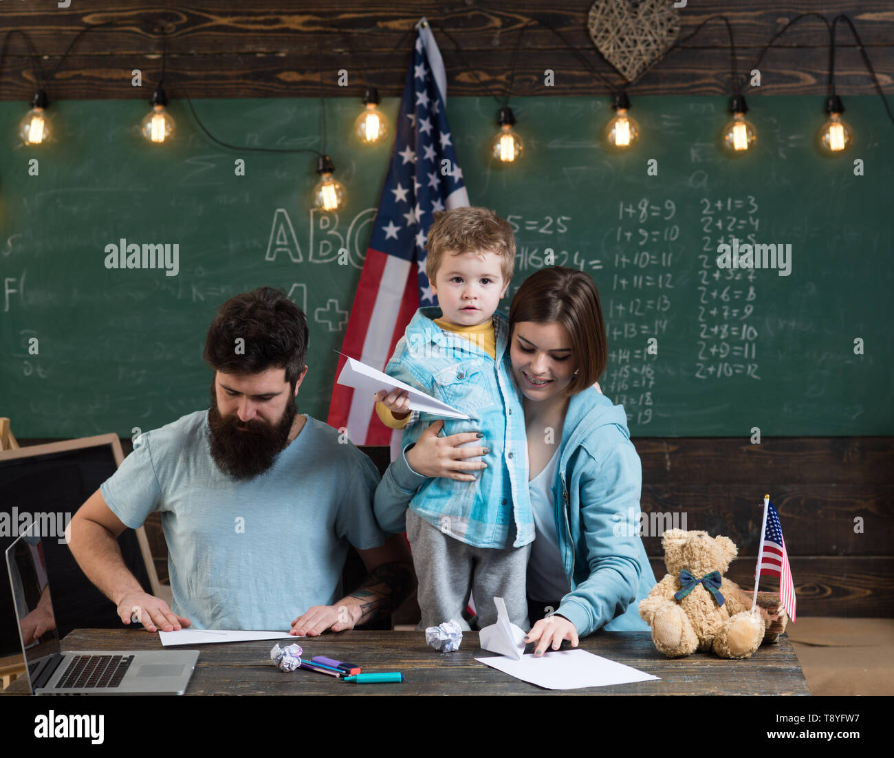 American family at desk with son making paper planes. Kid with parents ...