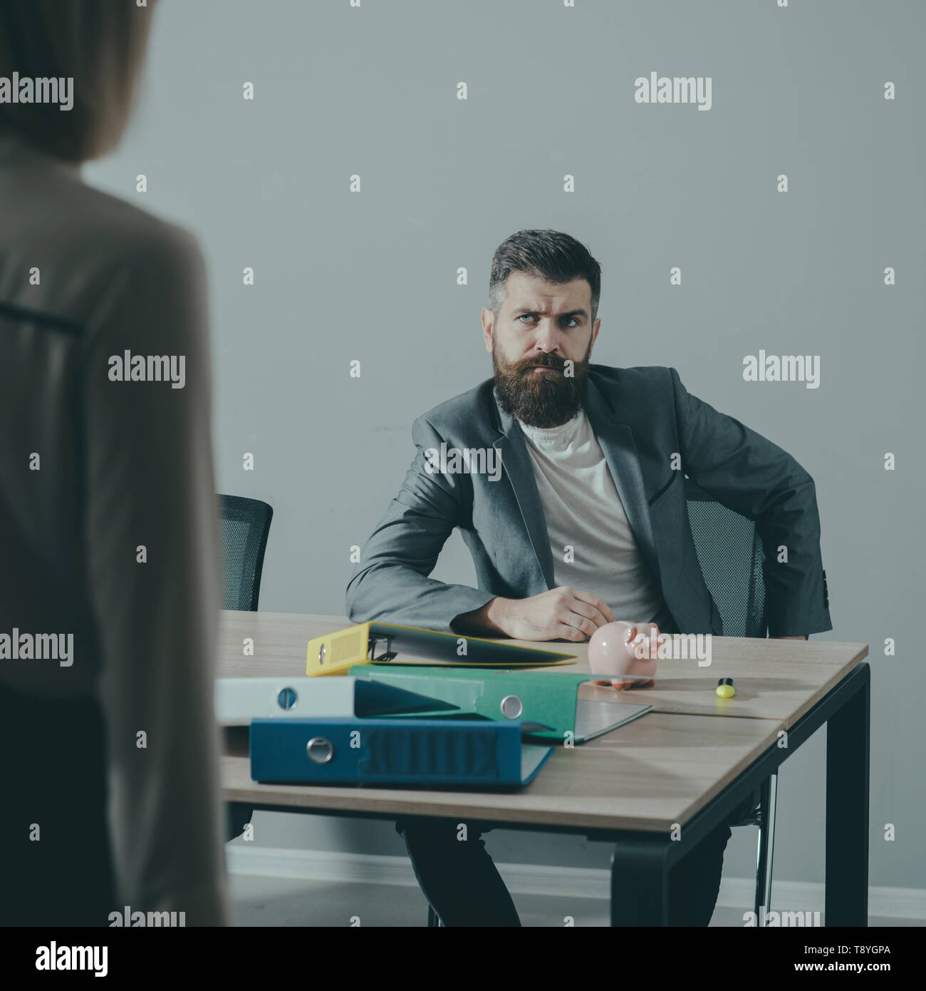 Serious boss look at blurred woman in foreground. Bearded man sit at ...