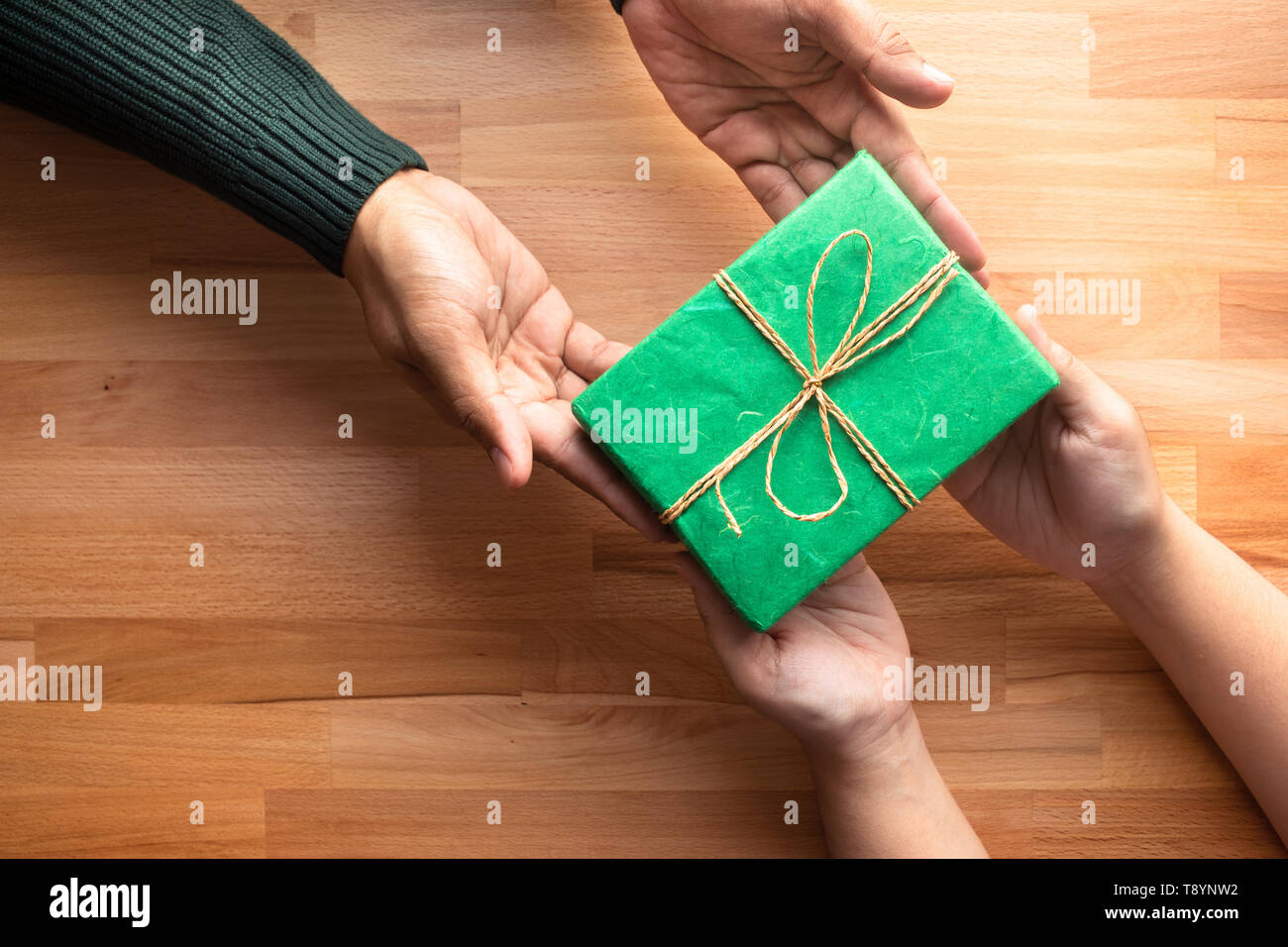 Male gives a gift present to female with wooden copy space background ...