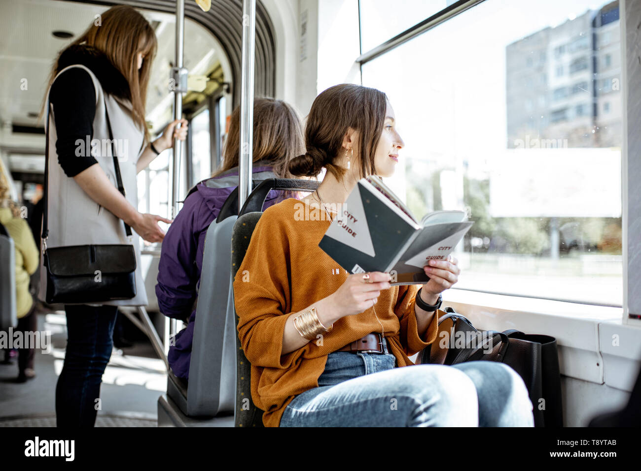 Young woman reading book while moving in the modern tram, happy ...