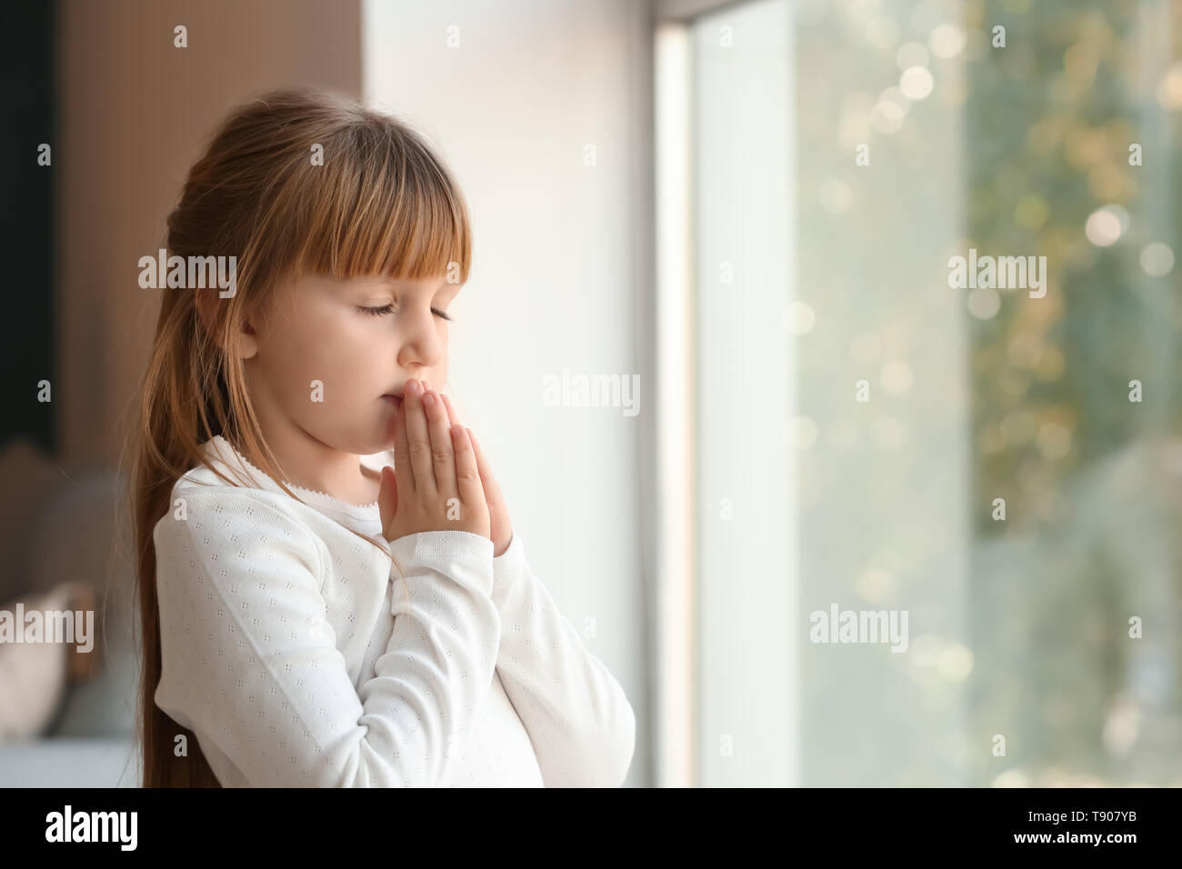 Little girl praying near window at home Stock Photo - Alamy