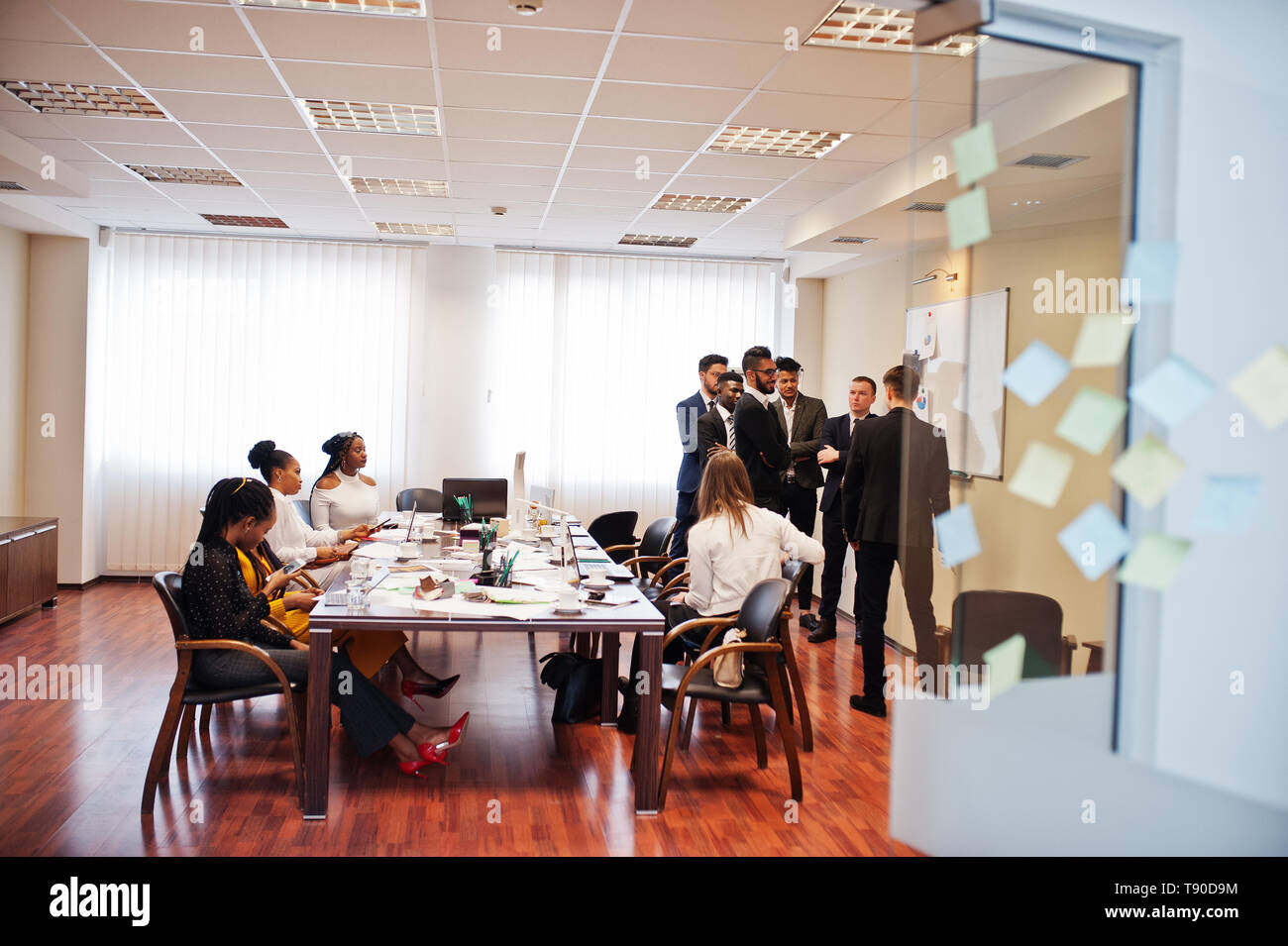 Multiracial business team addressing meeting around boardroom table and ...