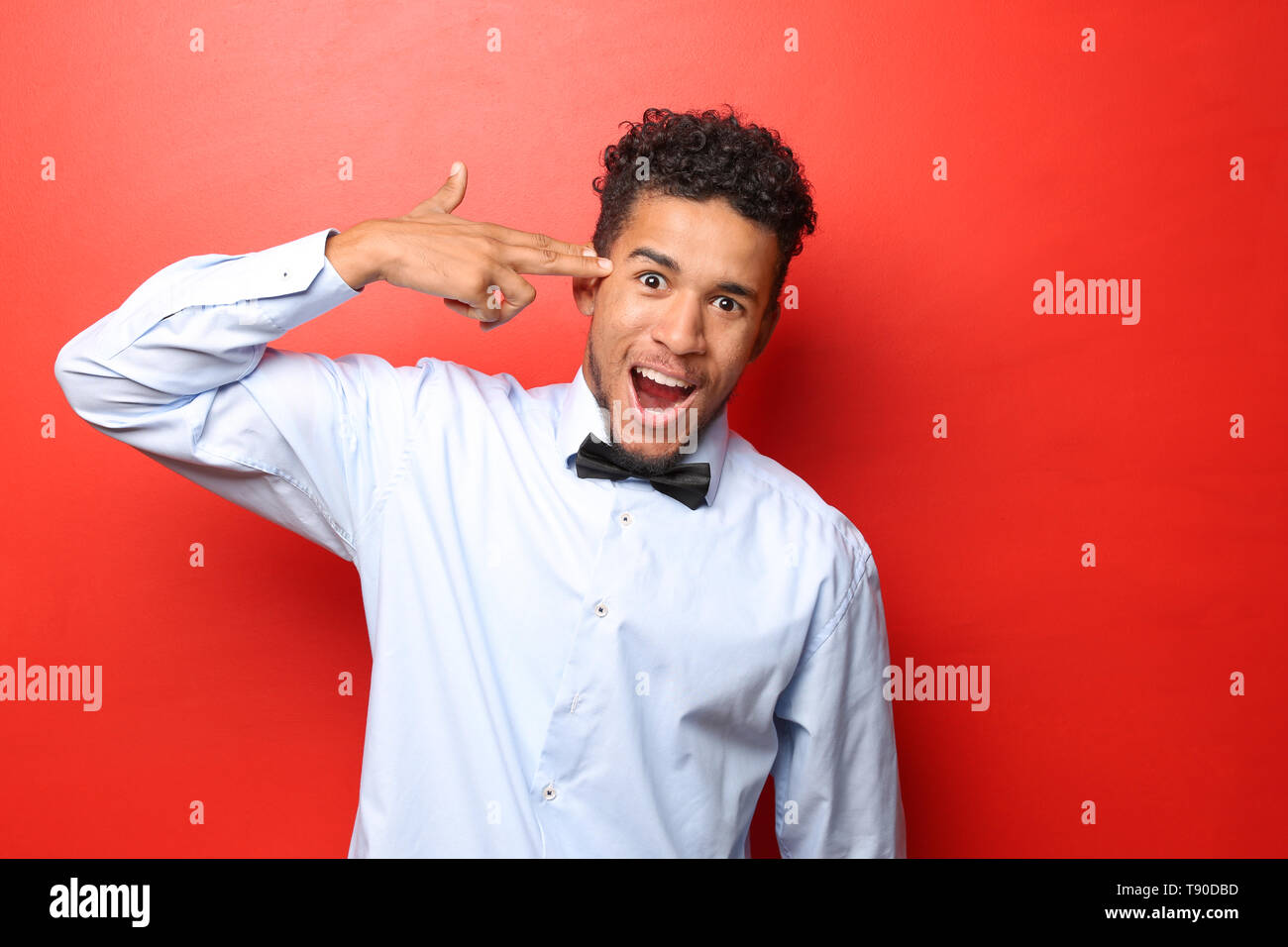 Portrait of African-American man showing "hand pistol" gesture on color ...
