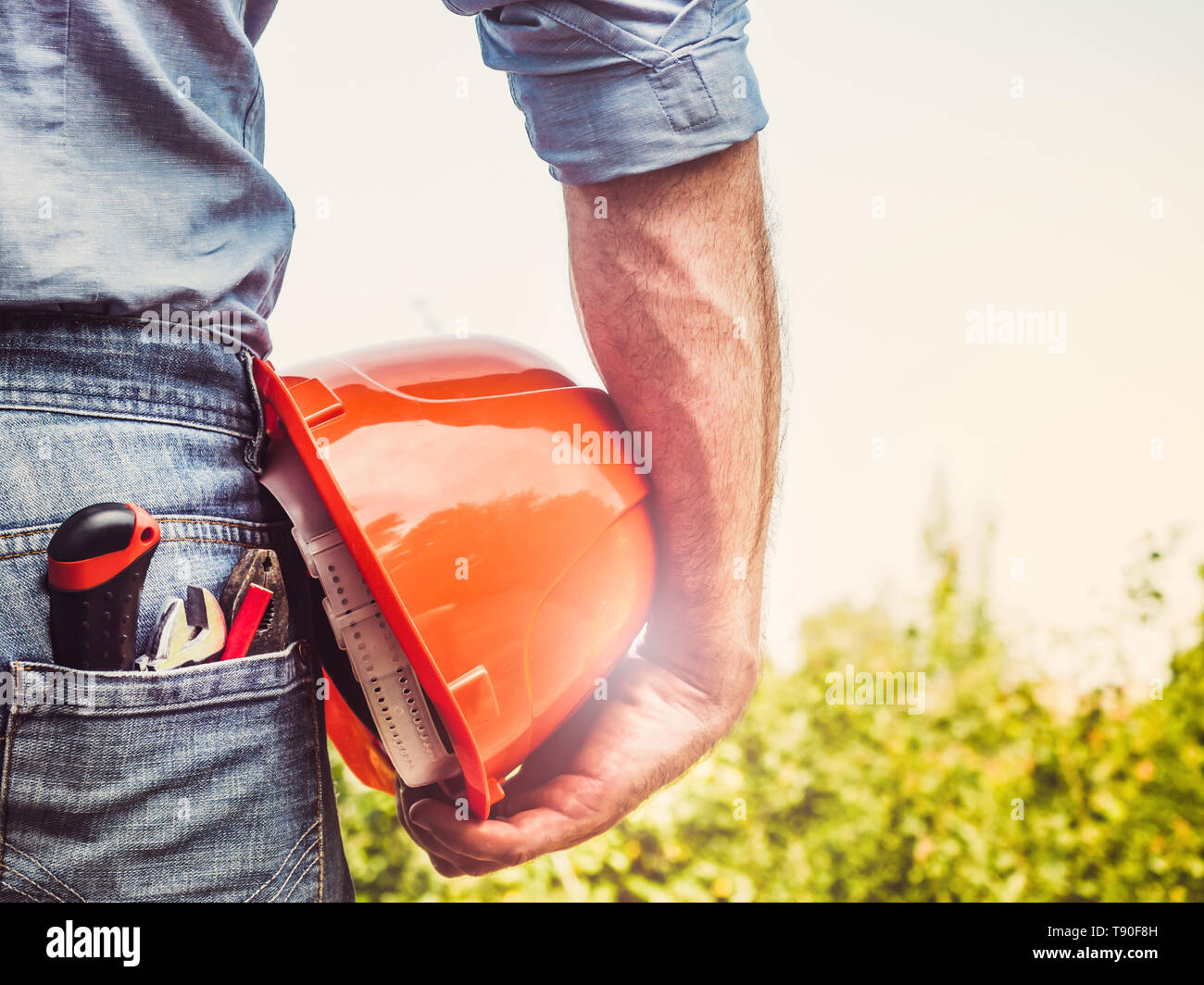 Handsome man with tools, standing against a background of green trees ...