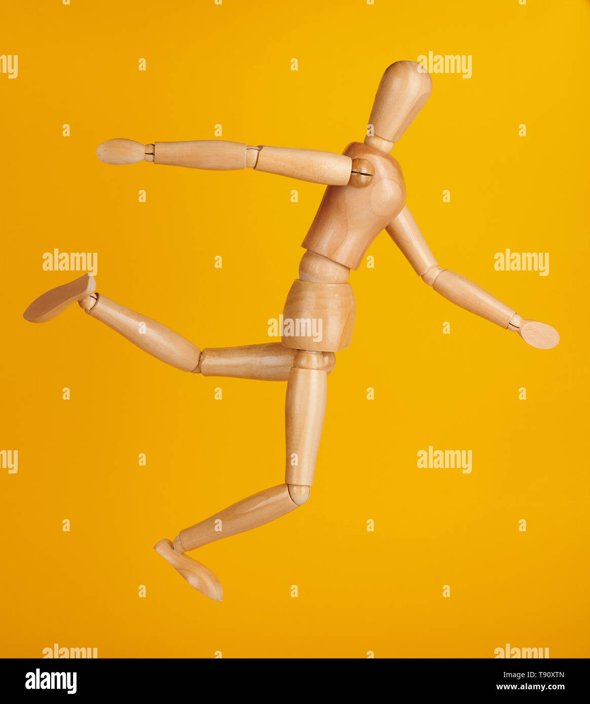 Wooden doll in kick ball pose side view isolated on yellow background ...