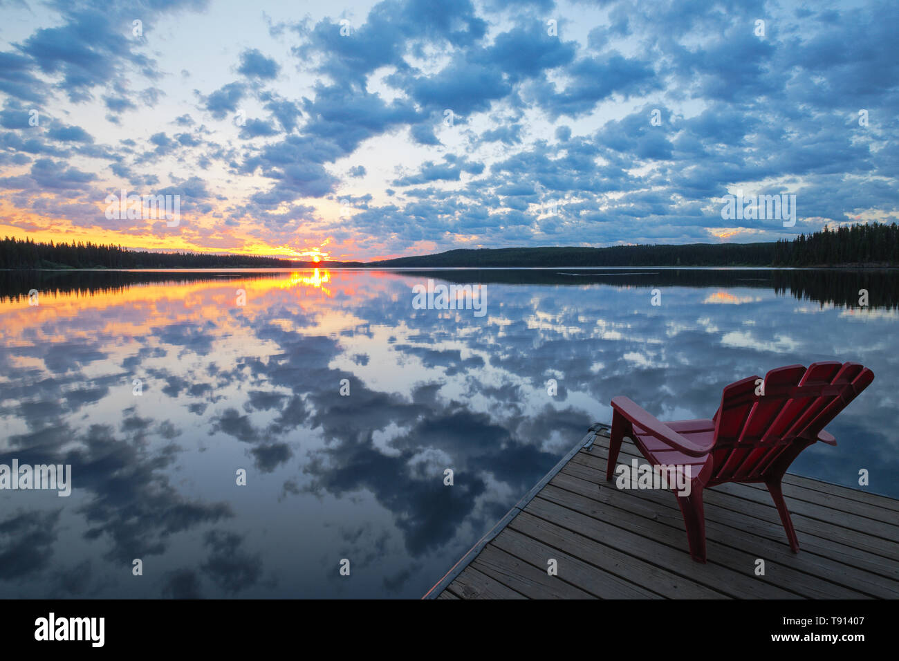 Red chair on a dock facing Beaver Lake reflecting the colourful sky at ...