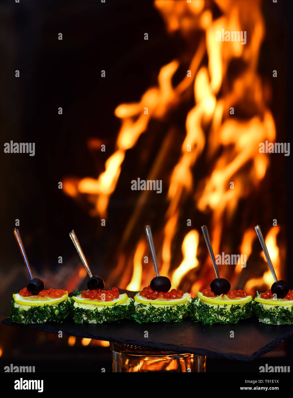 Snack food with red caviar and lemon on burning fire background. Caviar ...