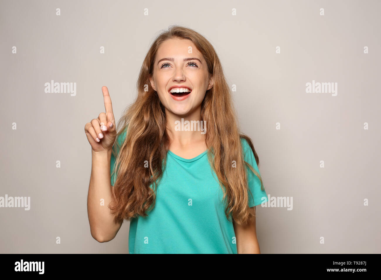 Portrait of beautiful young woman with raised index finger on light ...