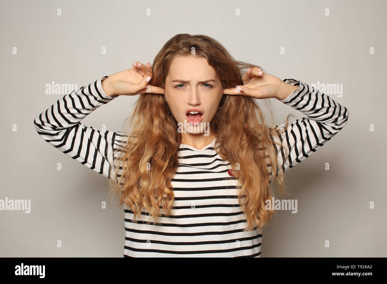 Portrait of beautiful young woman plugging ears on light background ...