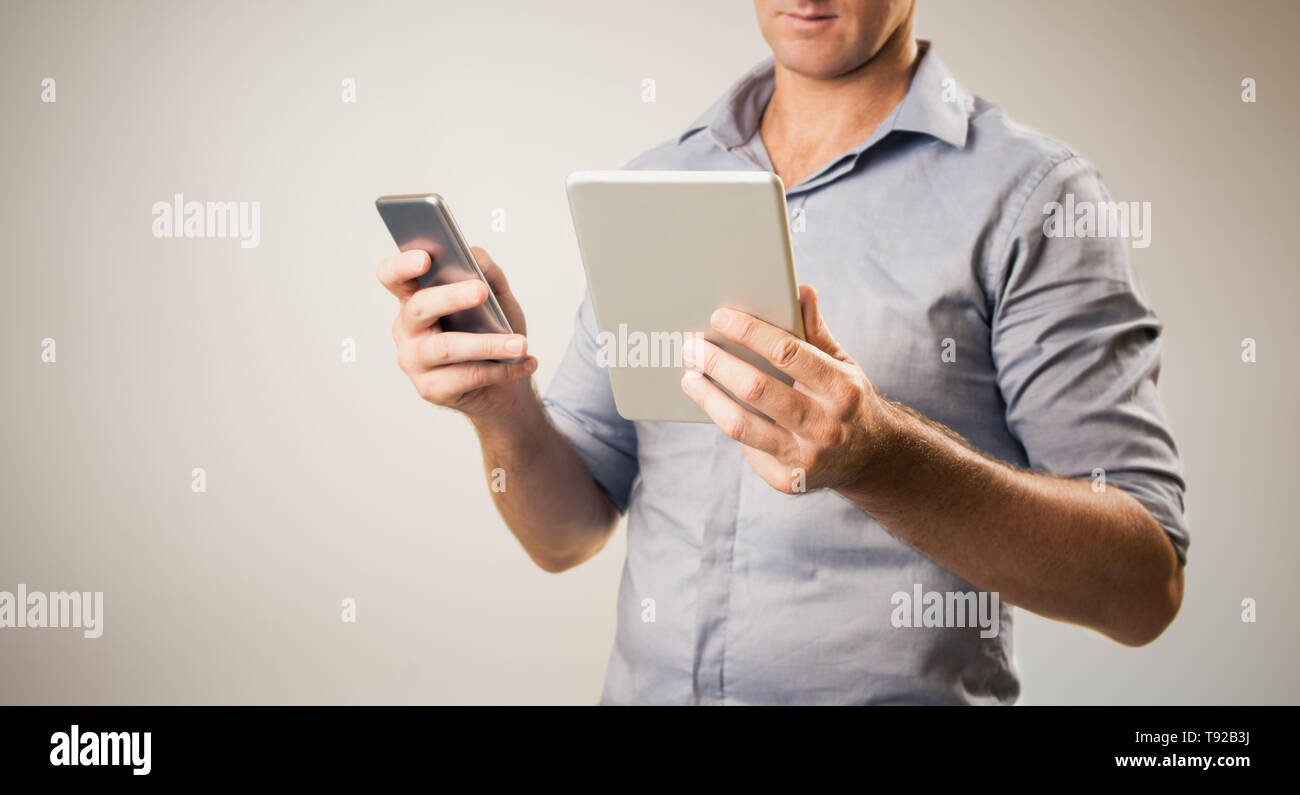 Man dressed casually in collared shirt using a tablet and phone ...
