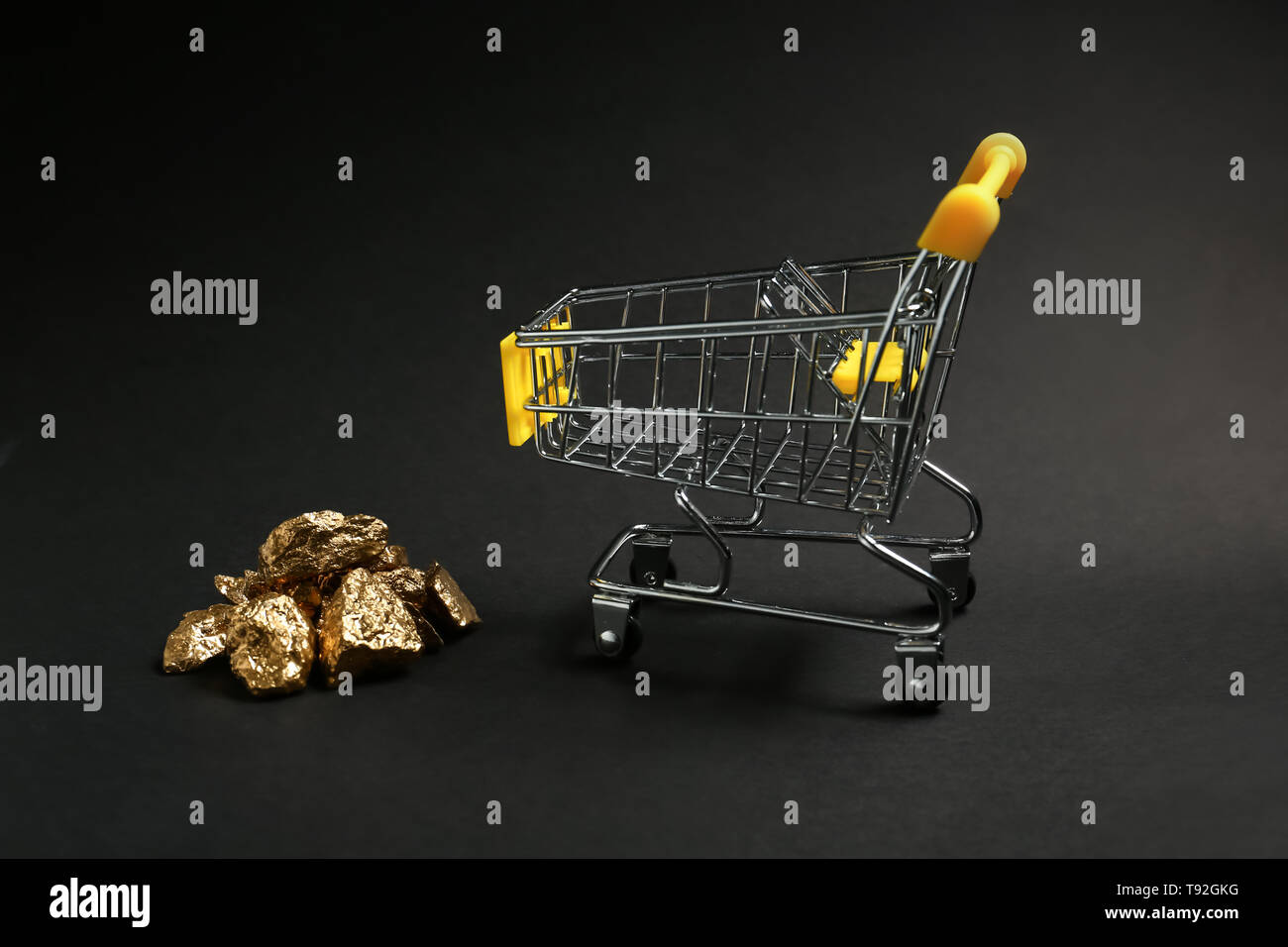 Small shopping cart and gold nuggets on dark background Stock Photo - Alamy