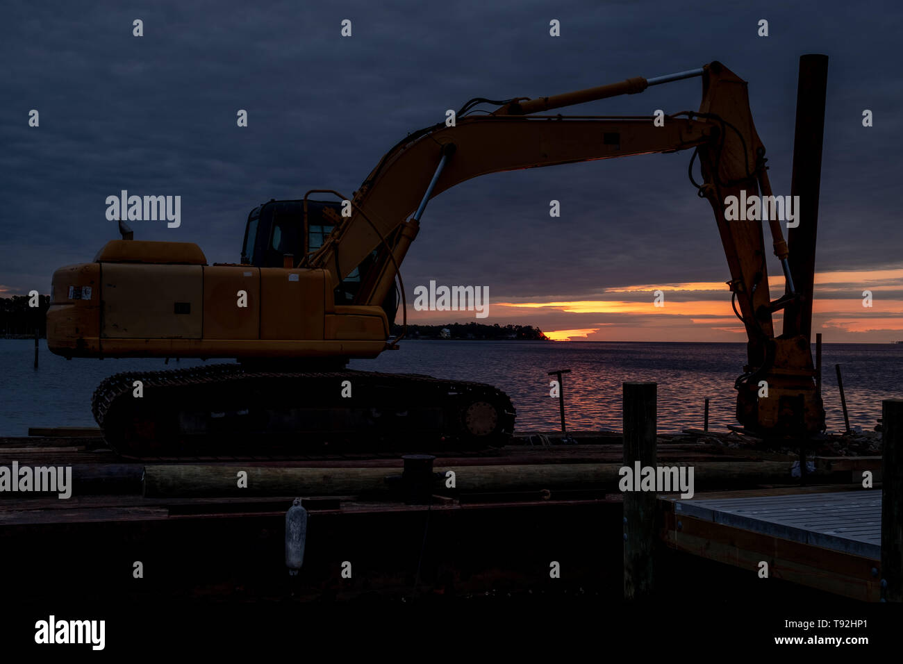 A pile driver rests on a floating platform by a pier after being used ...