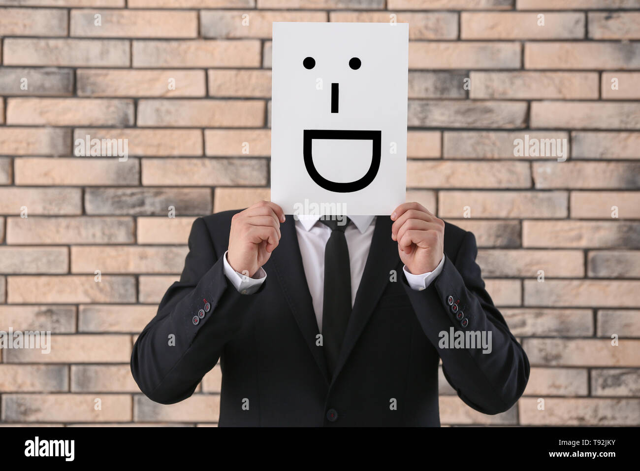 Businessman hiding face behind sheet of paper with drawn emoticon ...