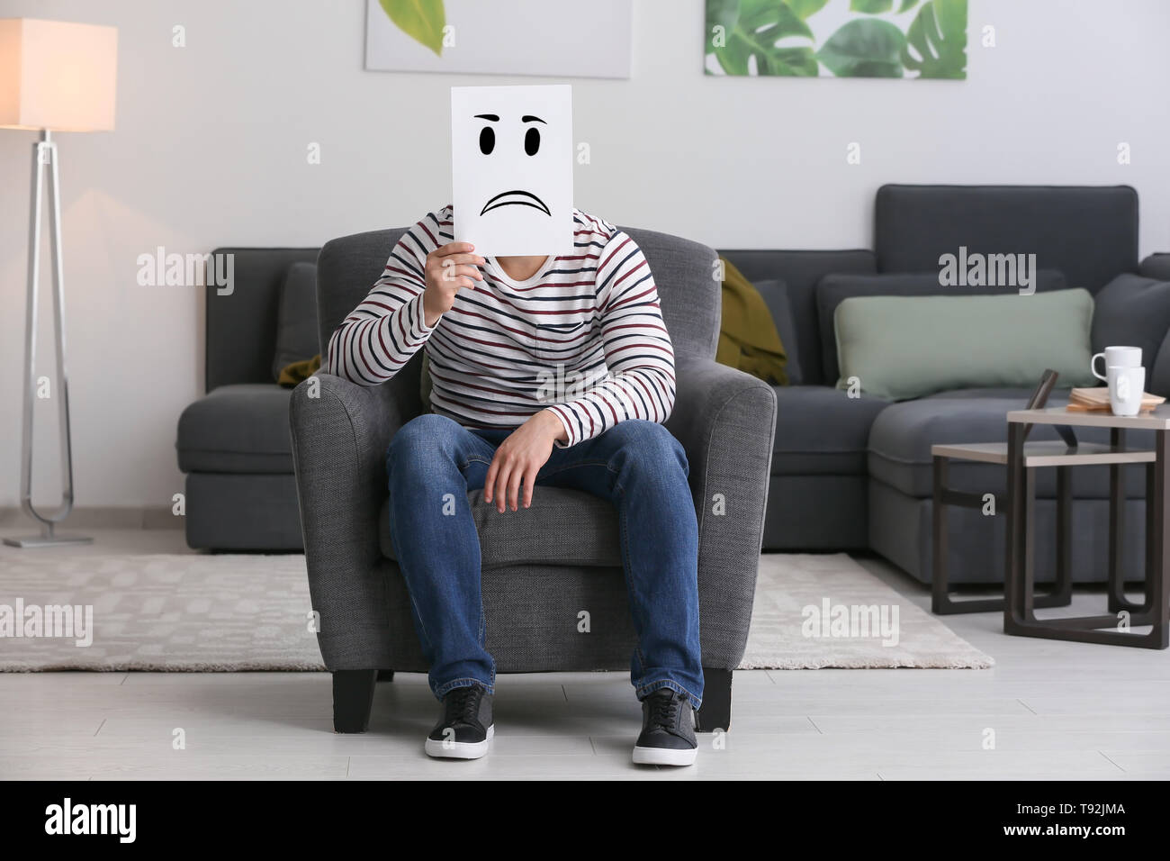 Young man hiding face behind sheet of paper with drawn emoticon while ...