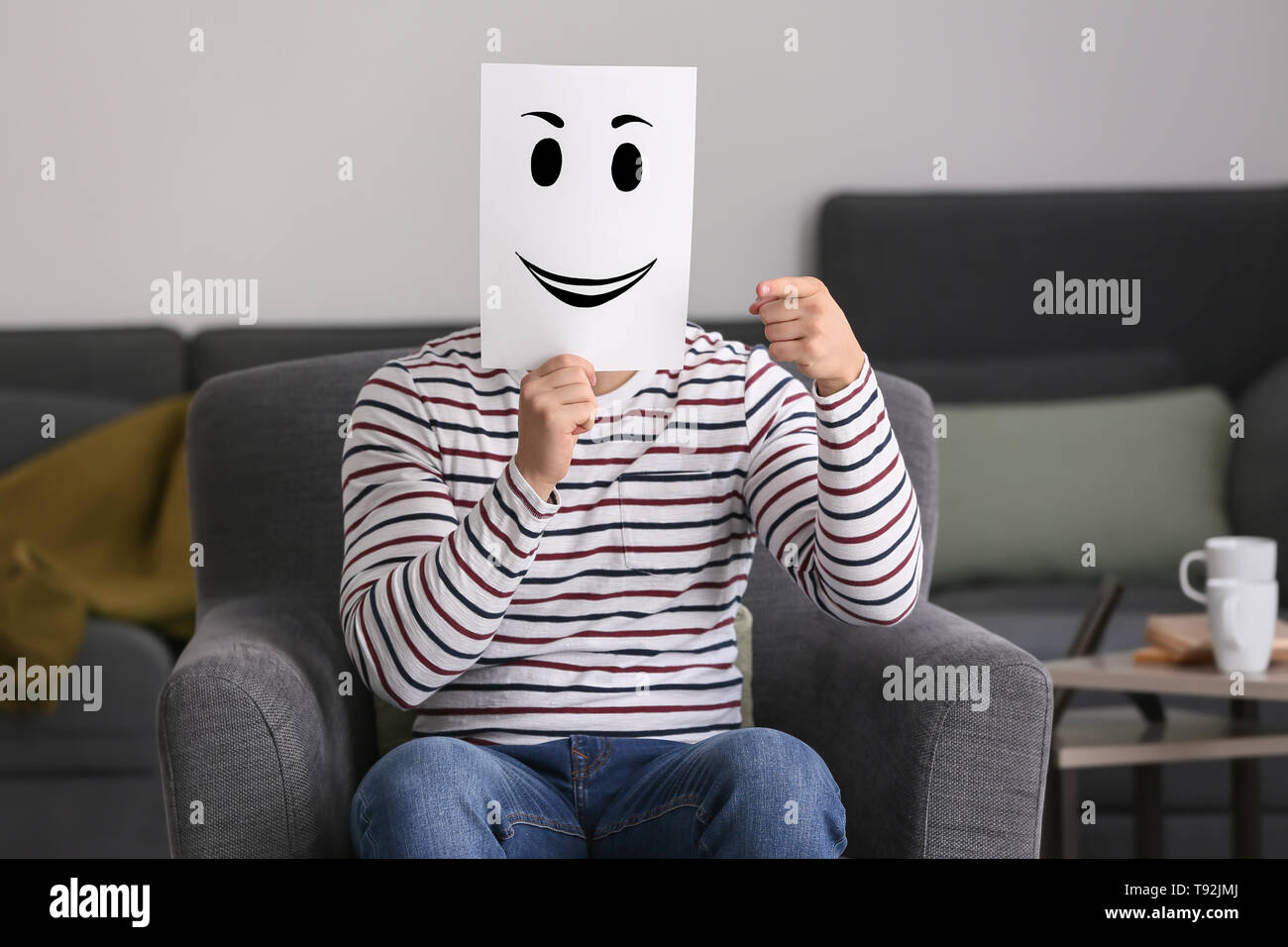 Young man hiding face behind sheet of paper with drawn emoticon while ...