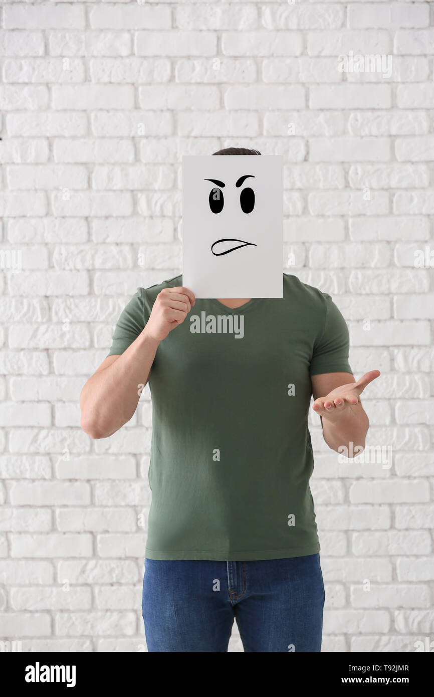 Young man hiding face behind sheet of paper with drawn emoticon against ...
