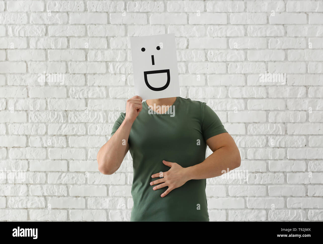 Young man hiding face behind sheet of paper with drawn emoticon against ...