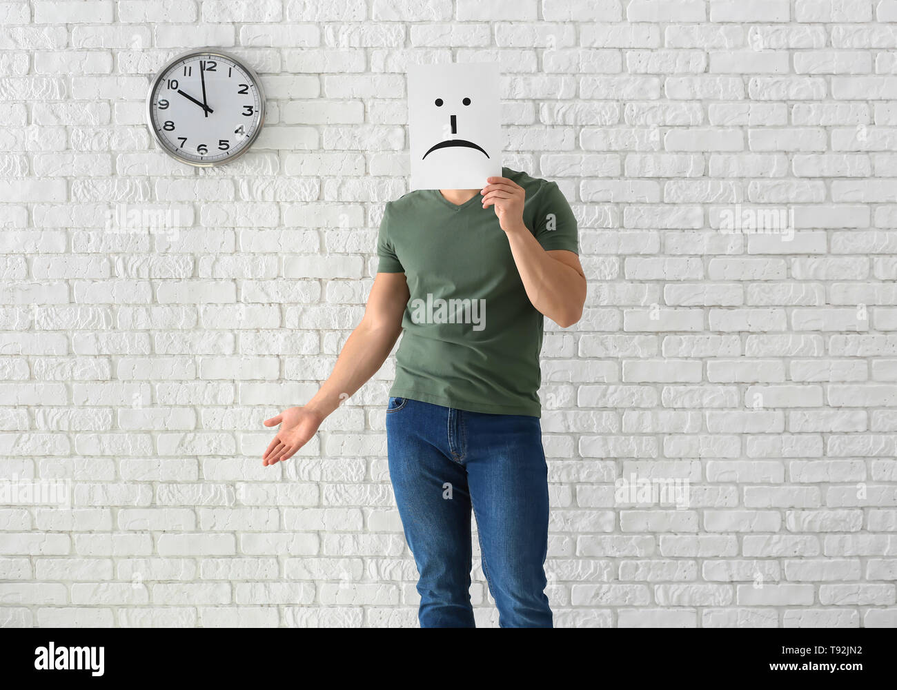 Young man hiding face behind sheet of paper with drawn emoticon against ...