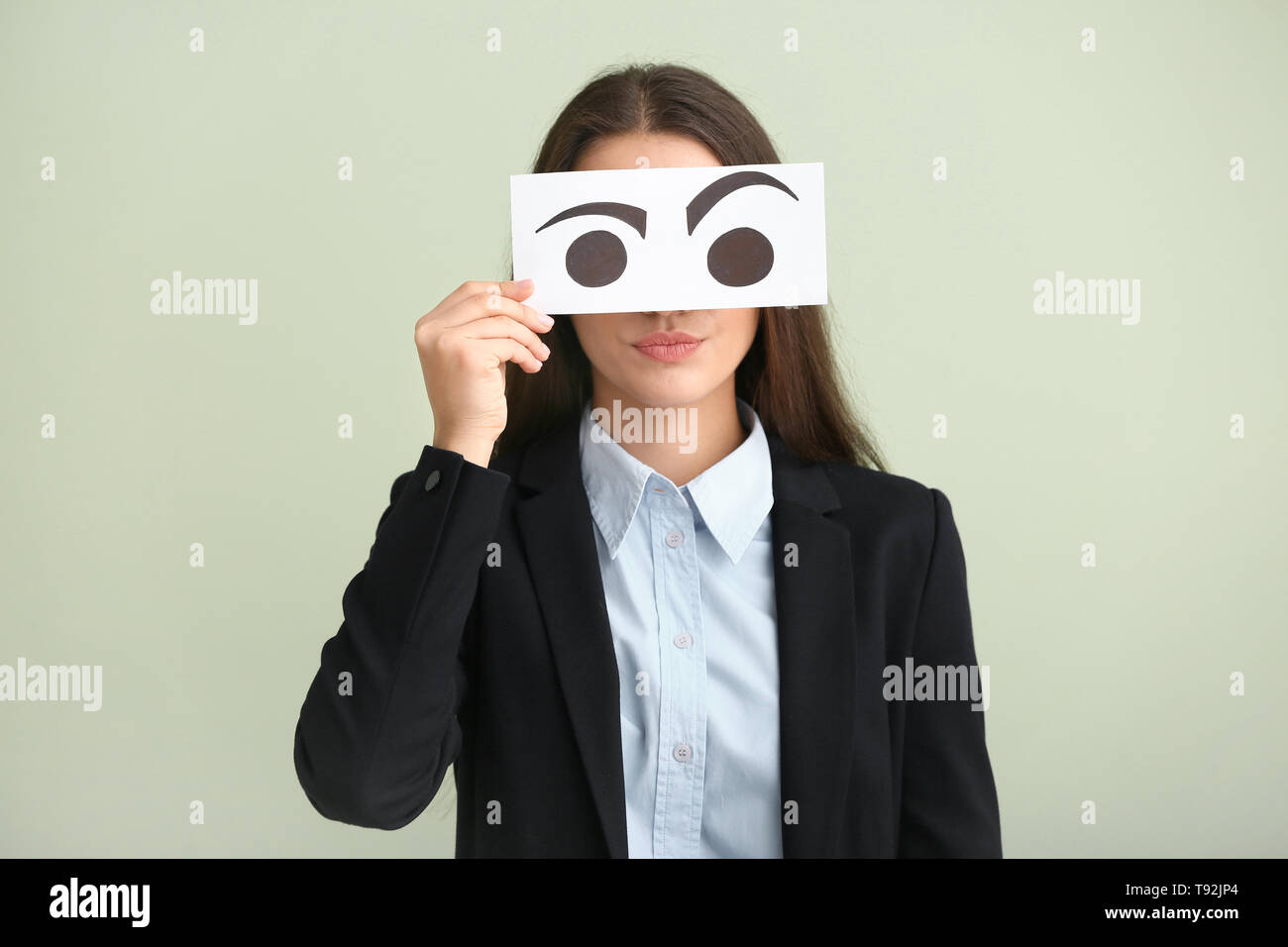 Emotional young woman hiding face behind sheet of paper with drawn eyes ...