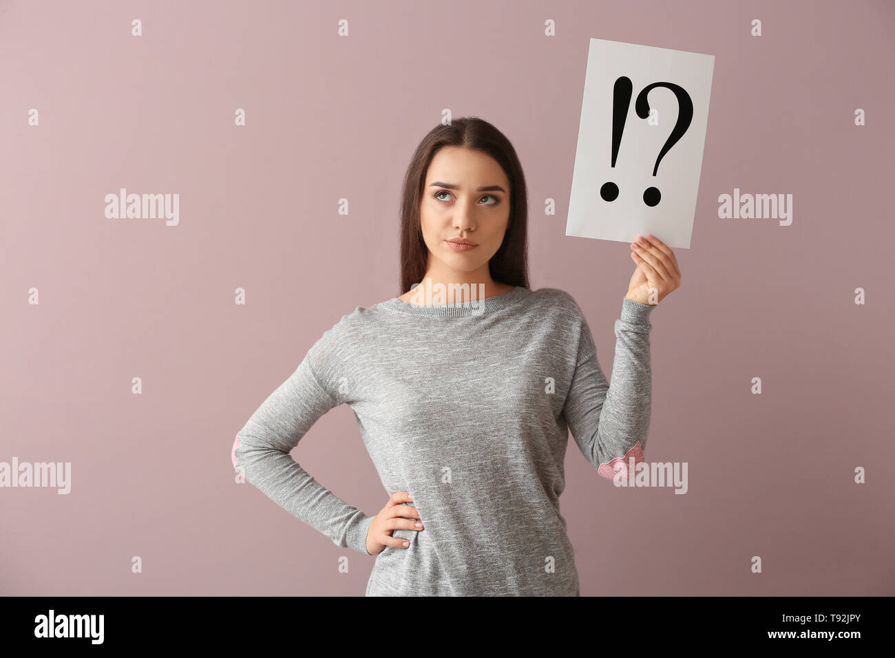 Thoughtful young woman holding sheet of paper with exclamation and ...