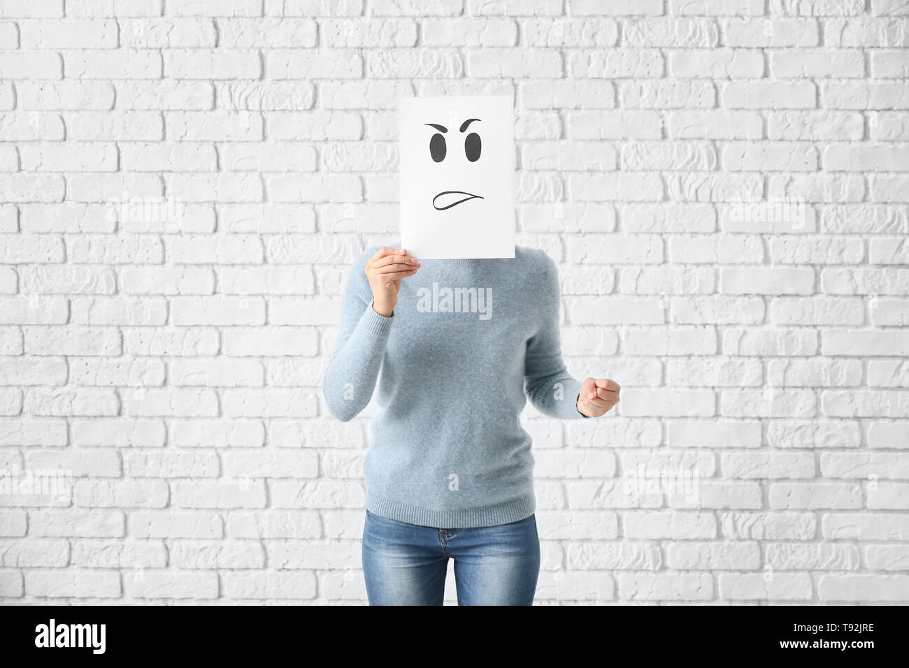 Young woman hiding face behind sheet of paper with drawn emoticon ...