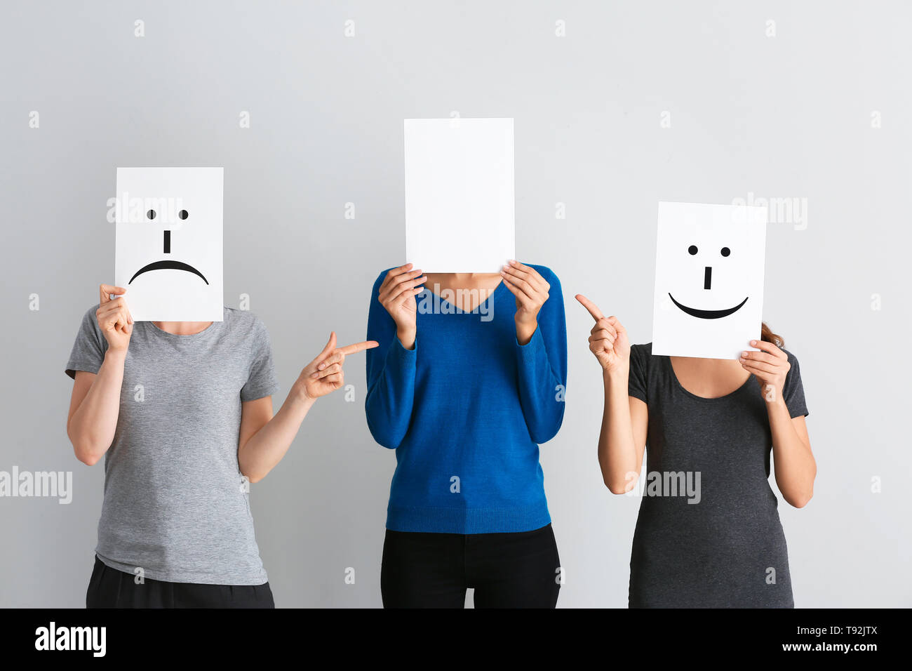 Young women hiding faces behind sheets of paper with drawn emoticons on ...
