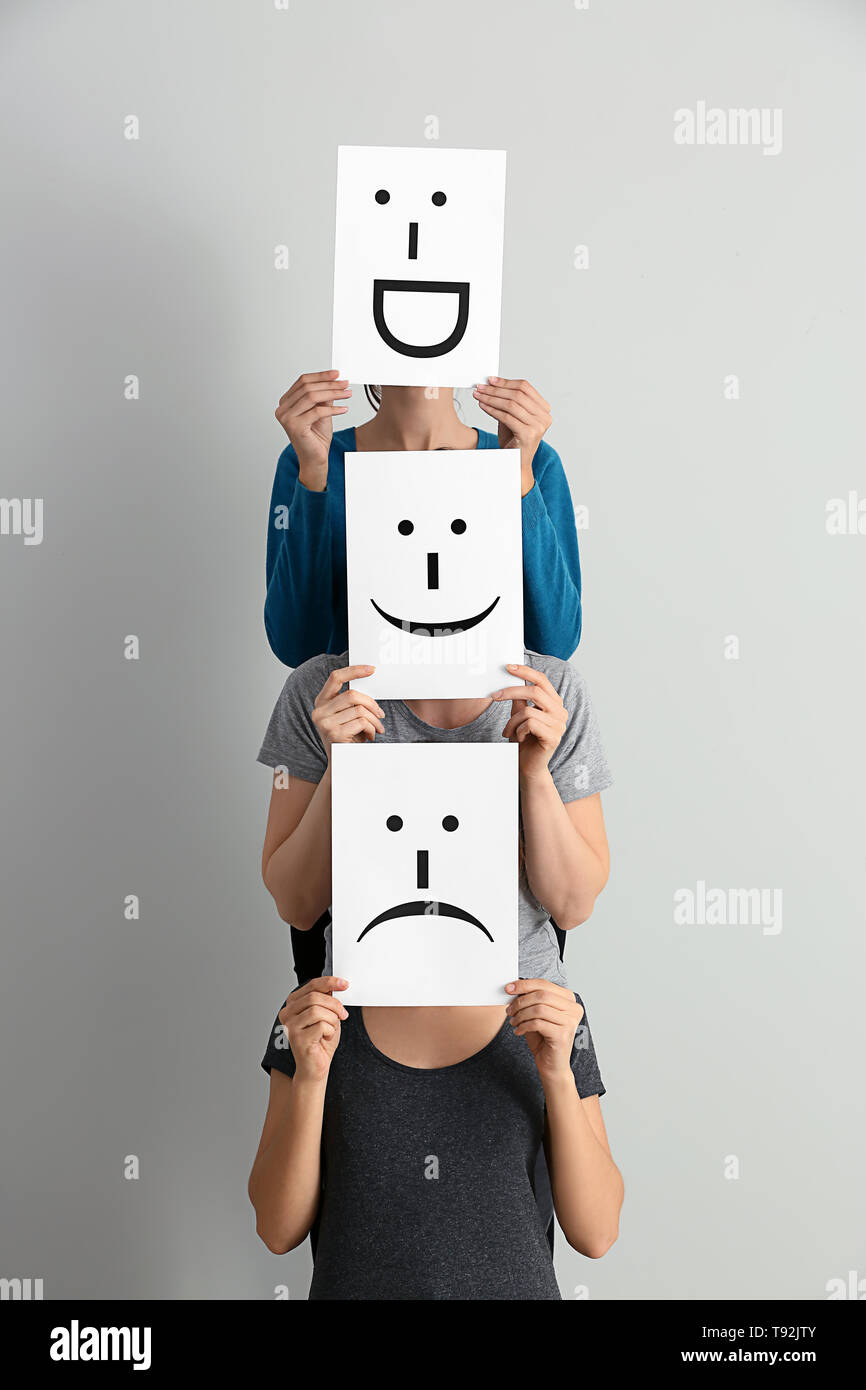 Young women hiding faces behind sheets of paper with drawn emoticons on ...