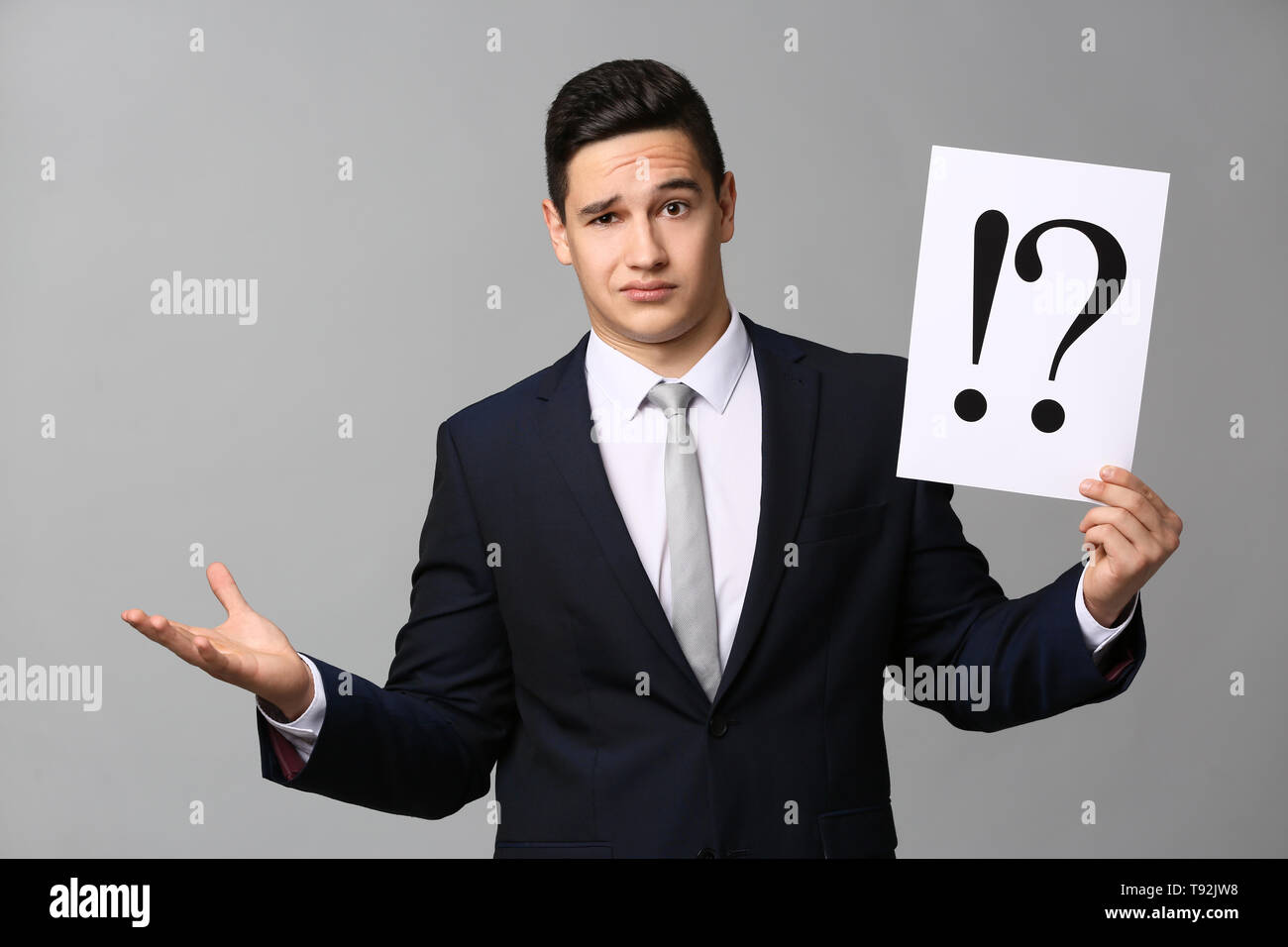 Emotional young businessman holding paper sheet with interrogation and ...