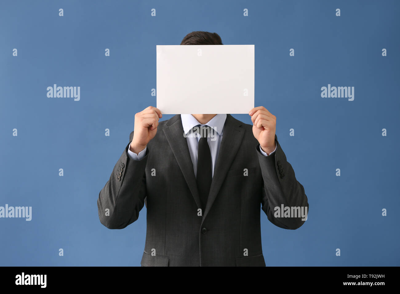 Unrecognizable businessman hiding face behind blank paper sheet hi-res ...