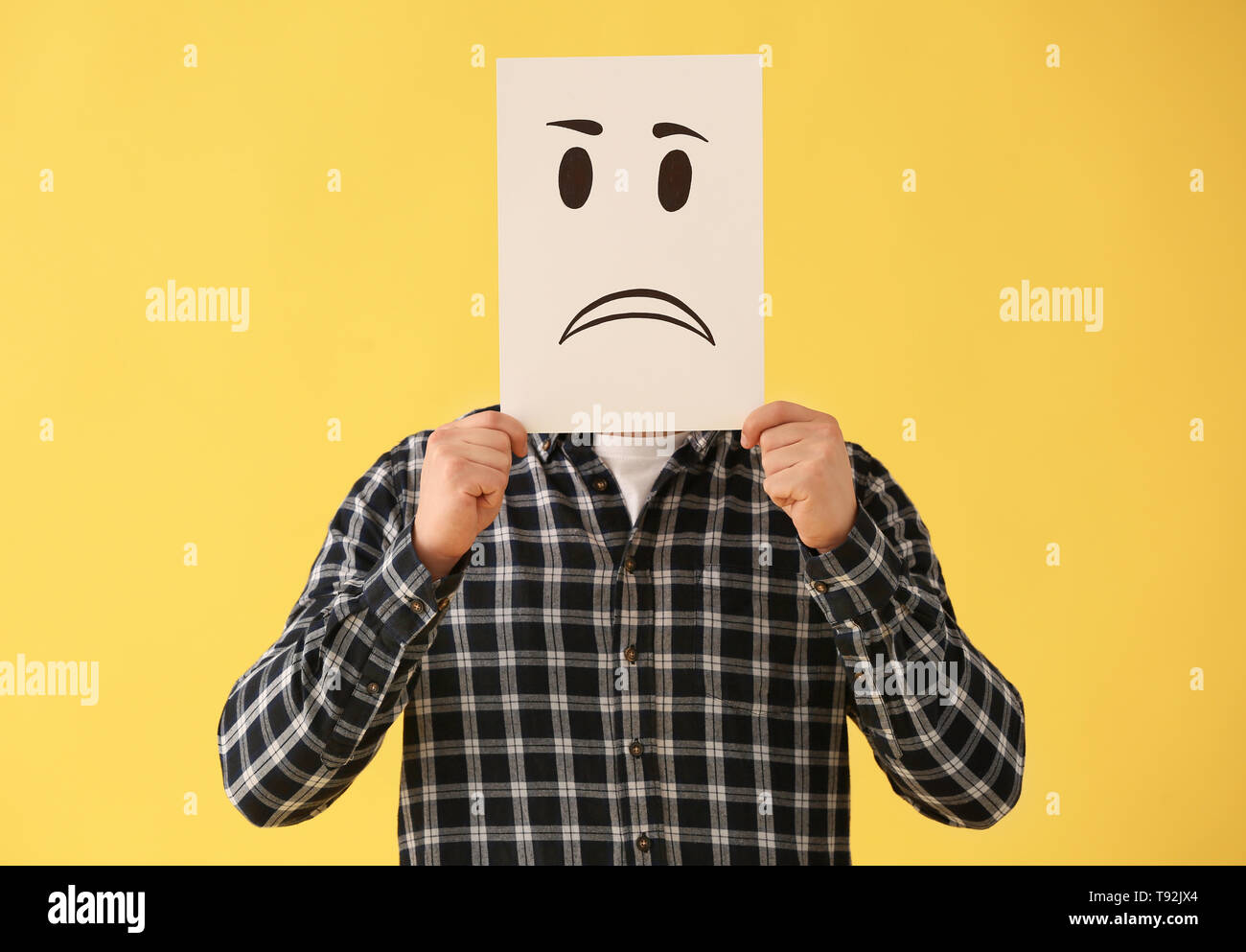 Man hiding face behind sheet of paper with drawn emoticon on color ...