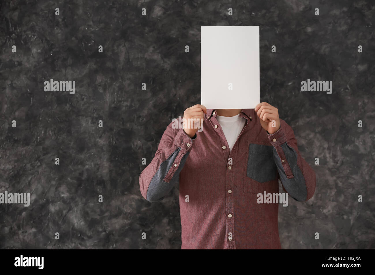 Young man hiding face behind blank sheet of paper on grey background ...
