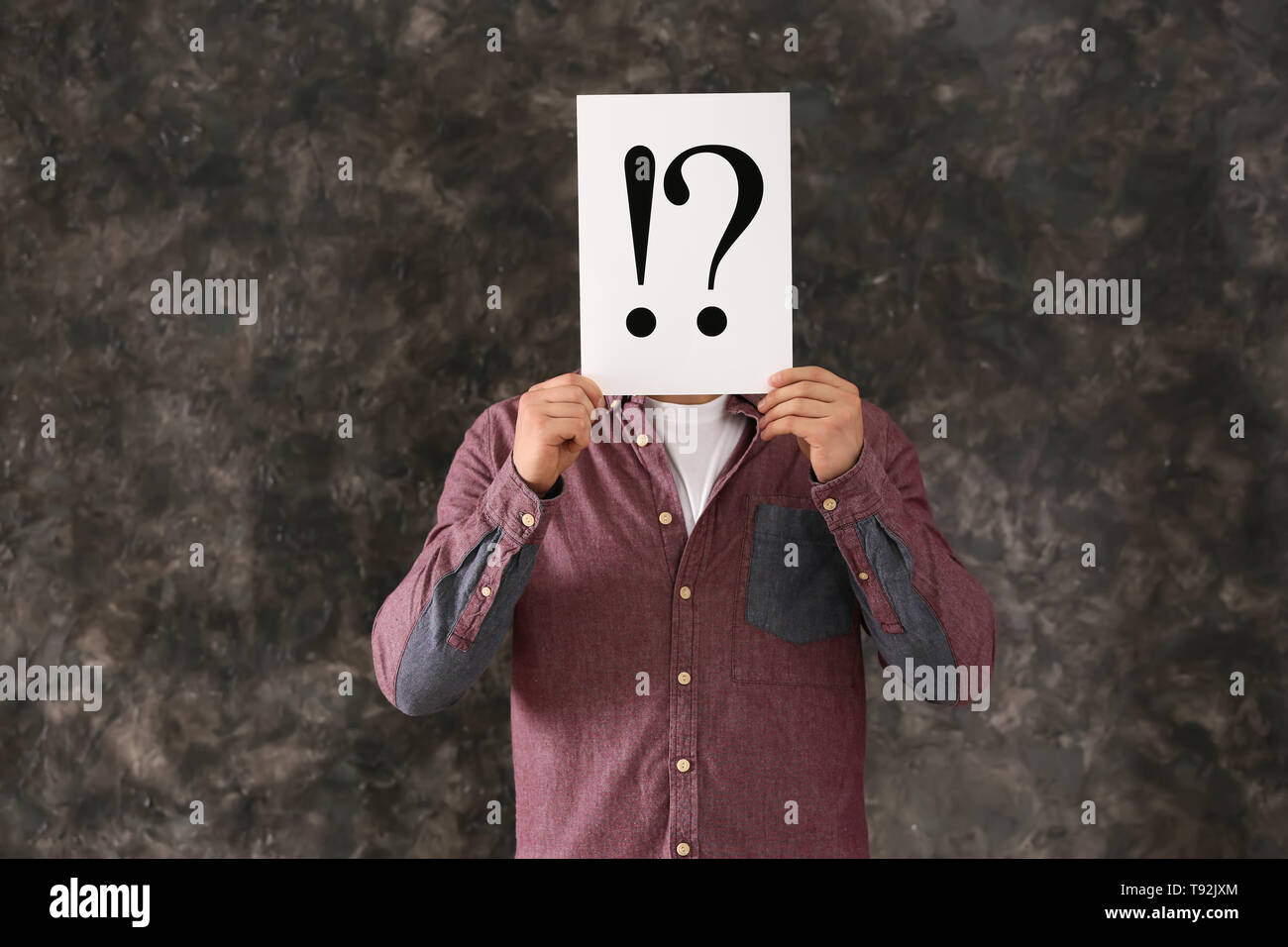 Young man hiding face behind sheet of paper with exclamation and ...