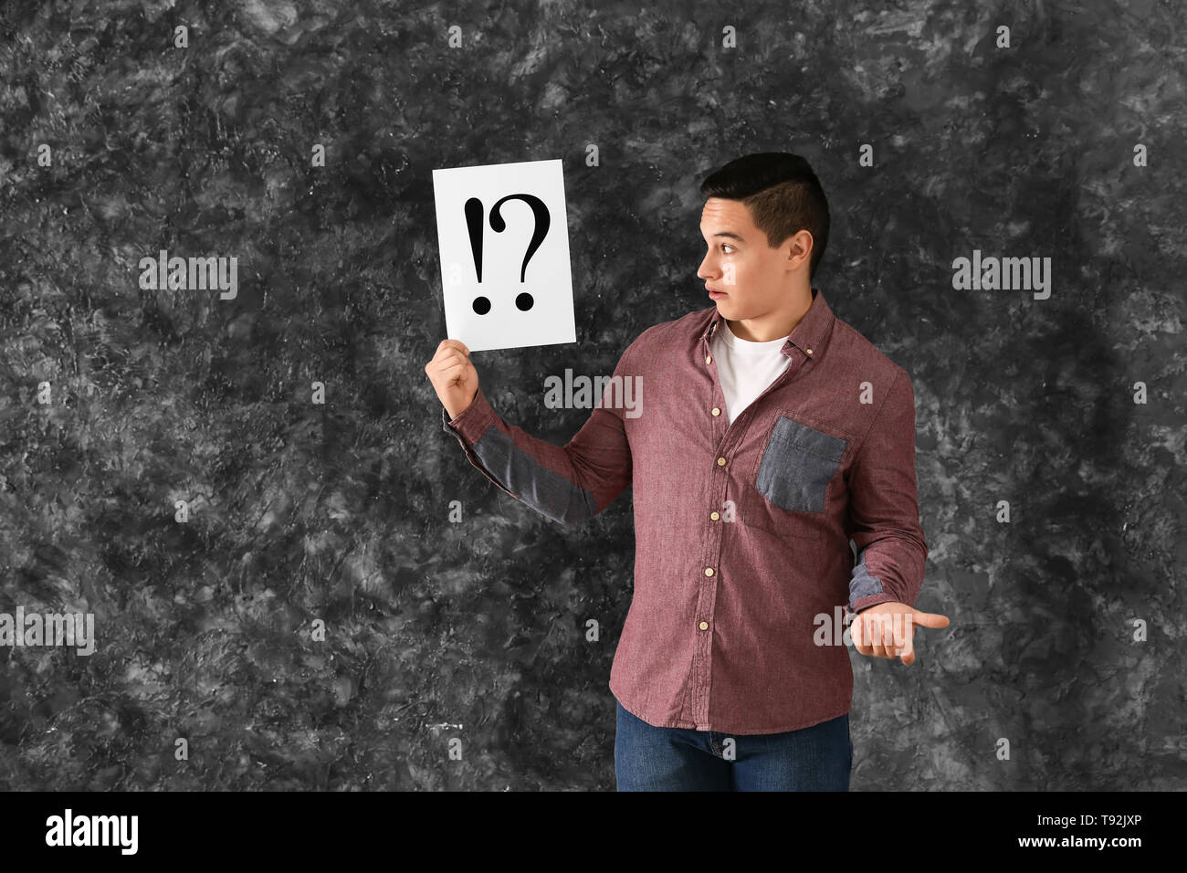 Young man holding sheet of paper with exclamation and interrogation ...