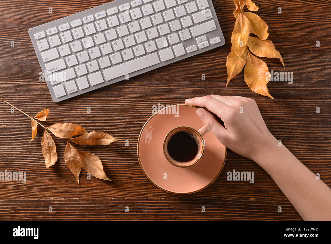 Woman with cup of aromatic coffee and computer keyboard at table, top ...