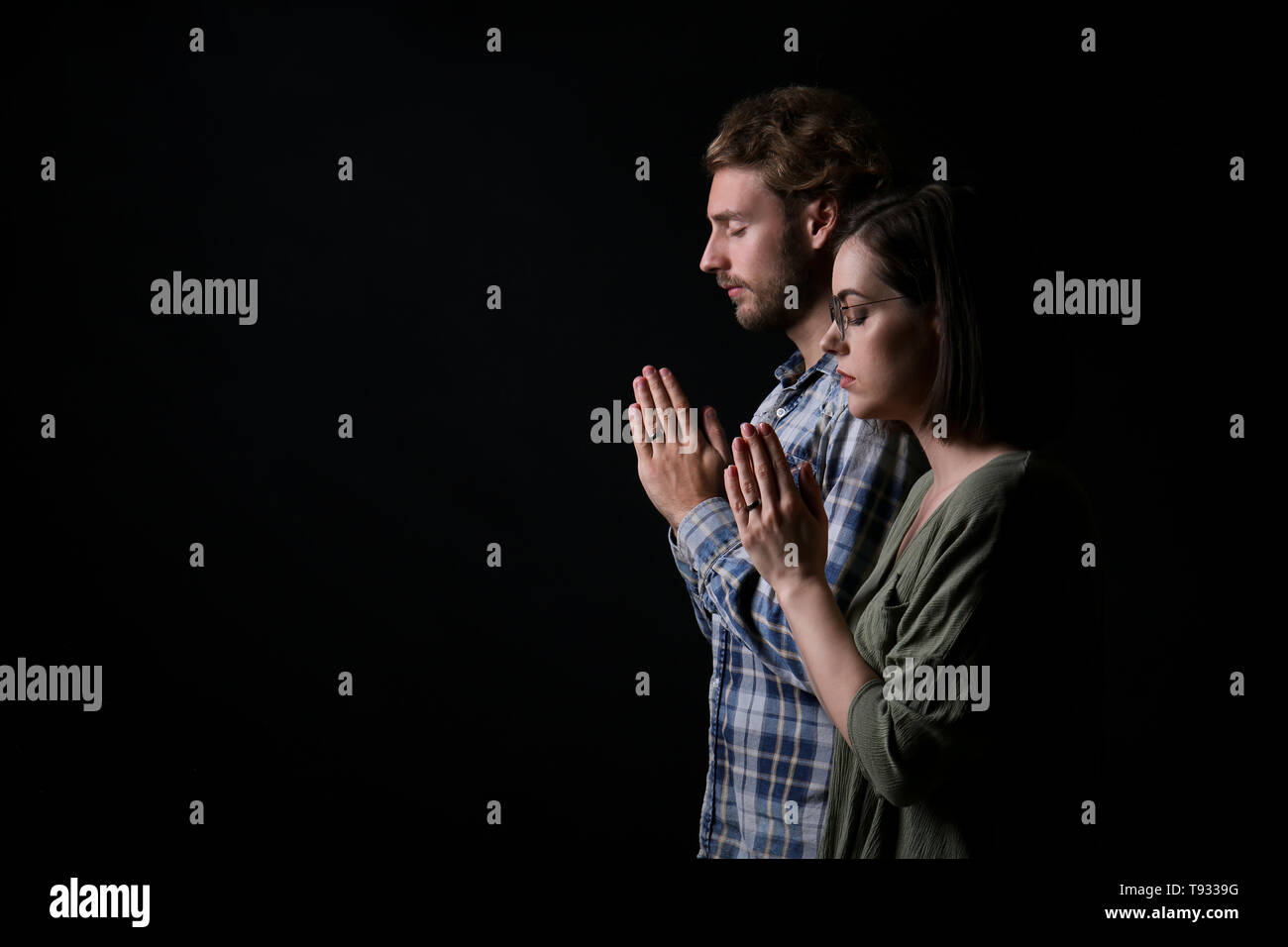 Young praying couple on dark background Stock Photo - Alamy
