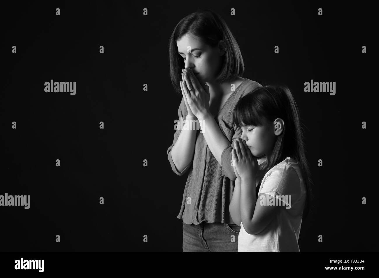 Praying mother and daughter on dark background Stock Photo - Alamy
