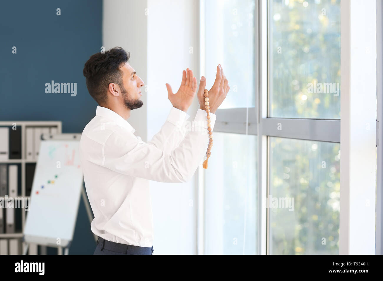 Young Muslim man praying near window Stock Photo - Alamy