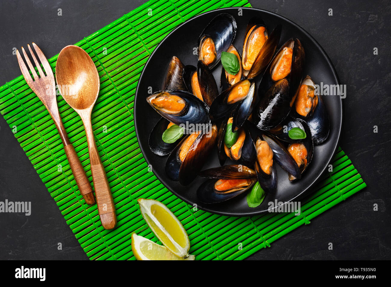 Seafood mussels and basil leaves in a black plate on bamboo mat and ...
