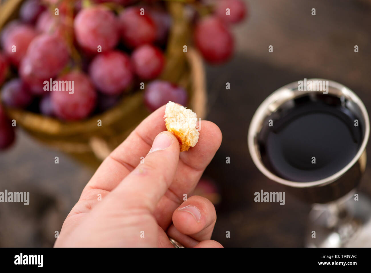 Man breaking the bread, with wine, grapes and Bible in the background ...