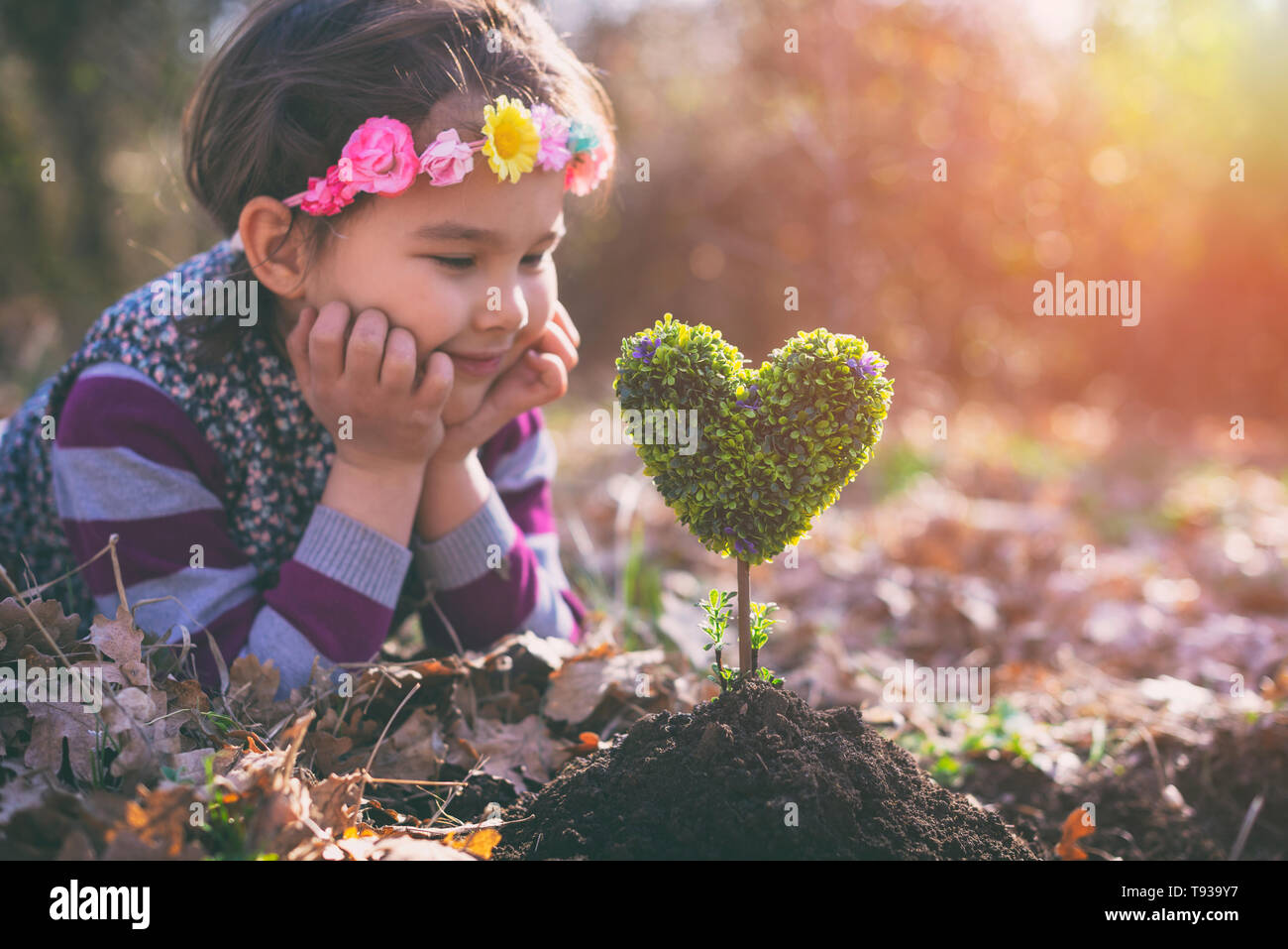 Beautiful little girl planting a heart-shaped tree and dreaming of a ...